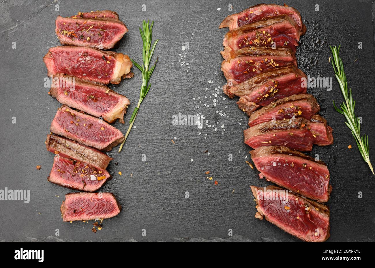 two fried beef steaks cut into pieces on a black board, the degree of ...