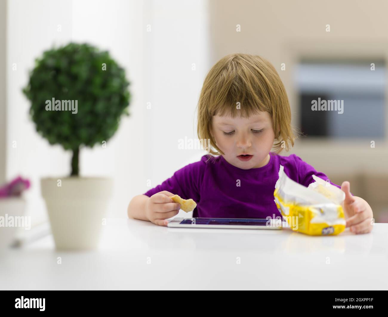 cute little girl eating a cookie while playing games on tablet computer ...