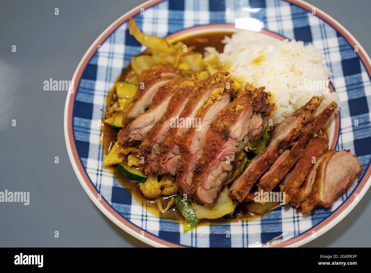 Crispy fried duck meal on vegetables with rice on a patterned plate in ...