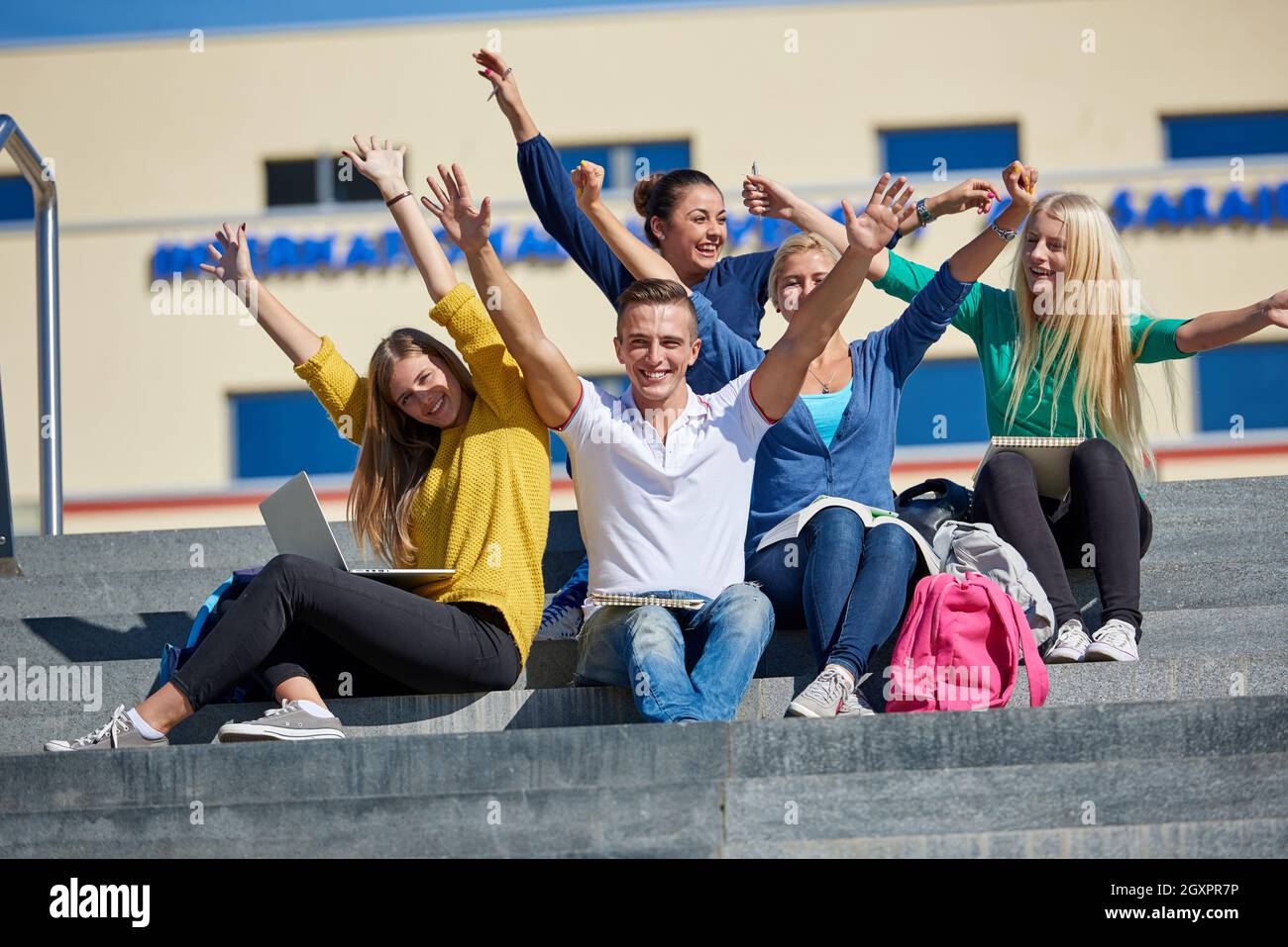 Group portrait of happy students outside in front of school sitting on ...