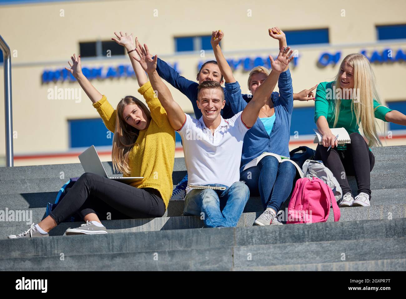Group portrait of happy students outside in front of school sitting on ...