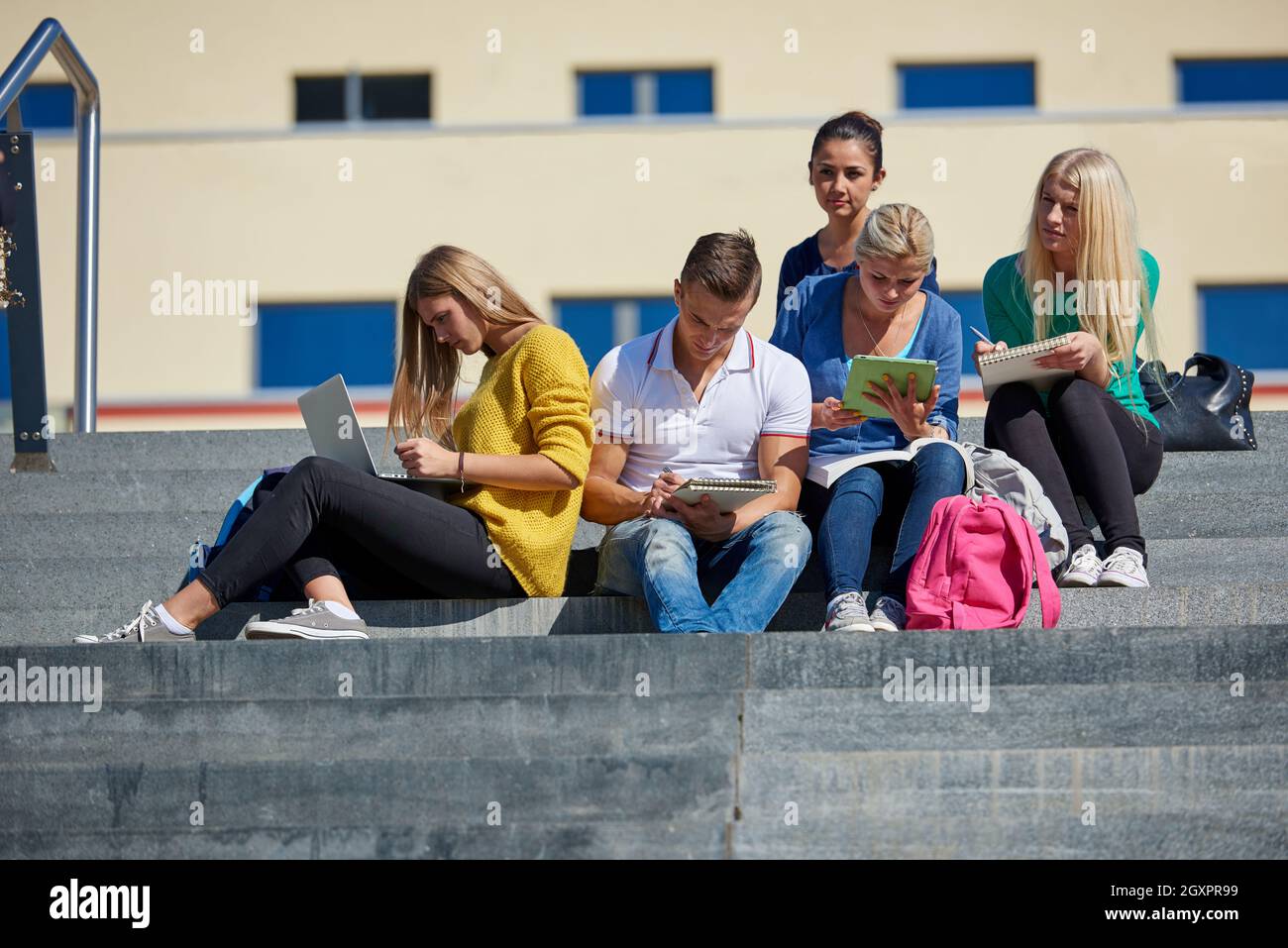 Group portrait of happy students outside in front of school sitting on ...