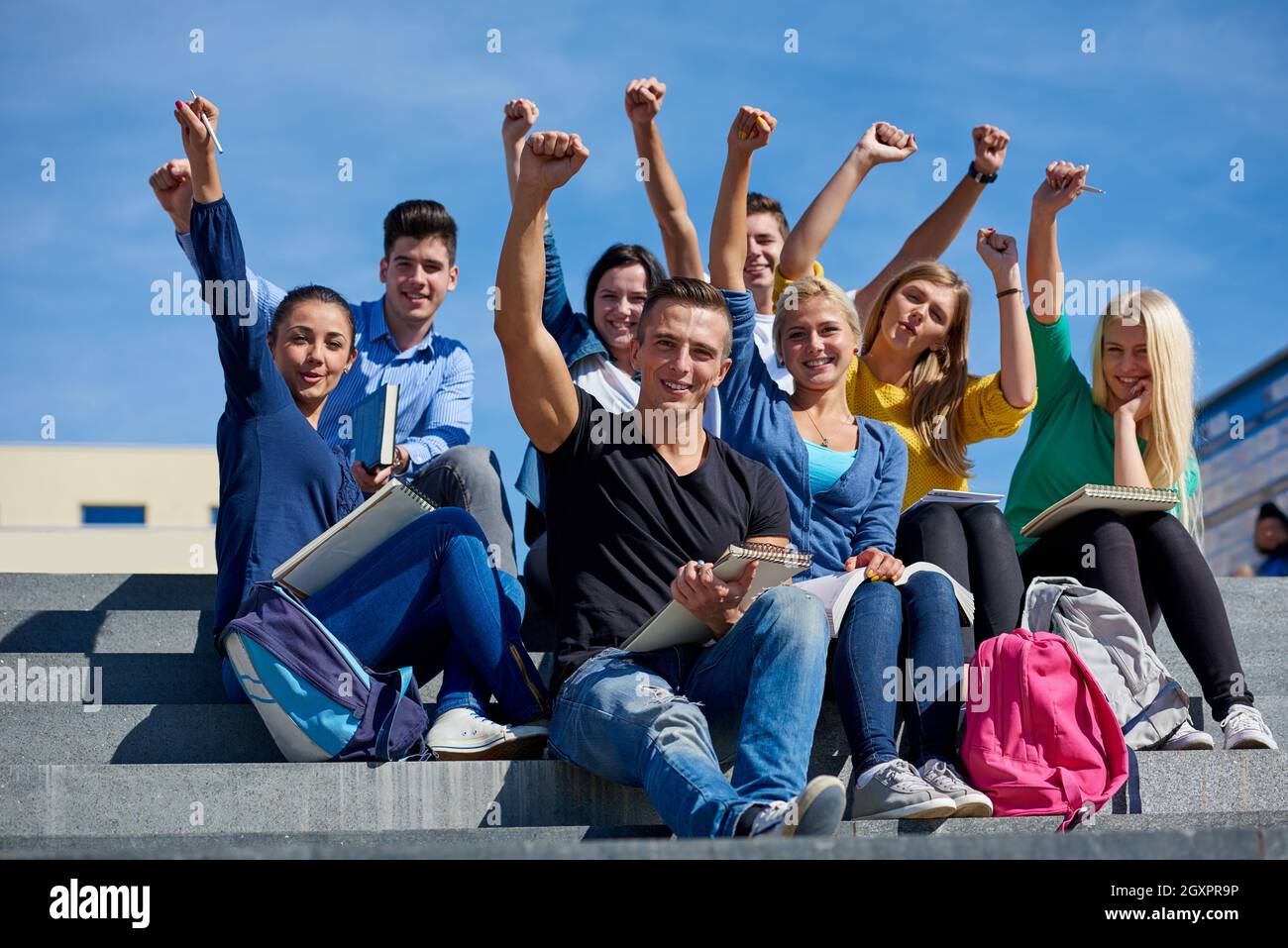 Group portrait of happy students outside in front of school sitting on ...