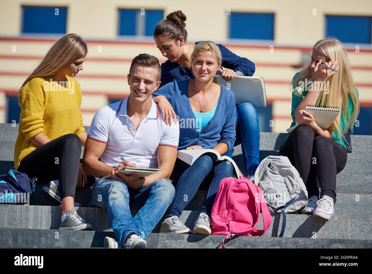 Group portrait of happy students outside in front of school sitting on ...