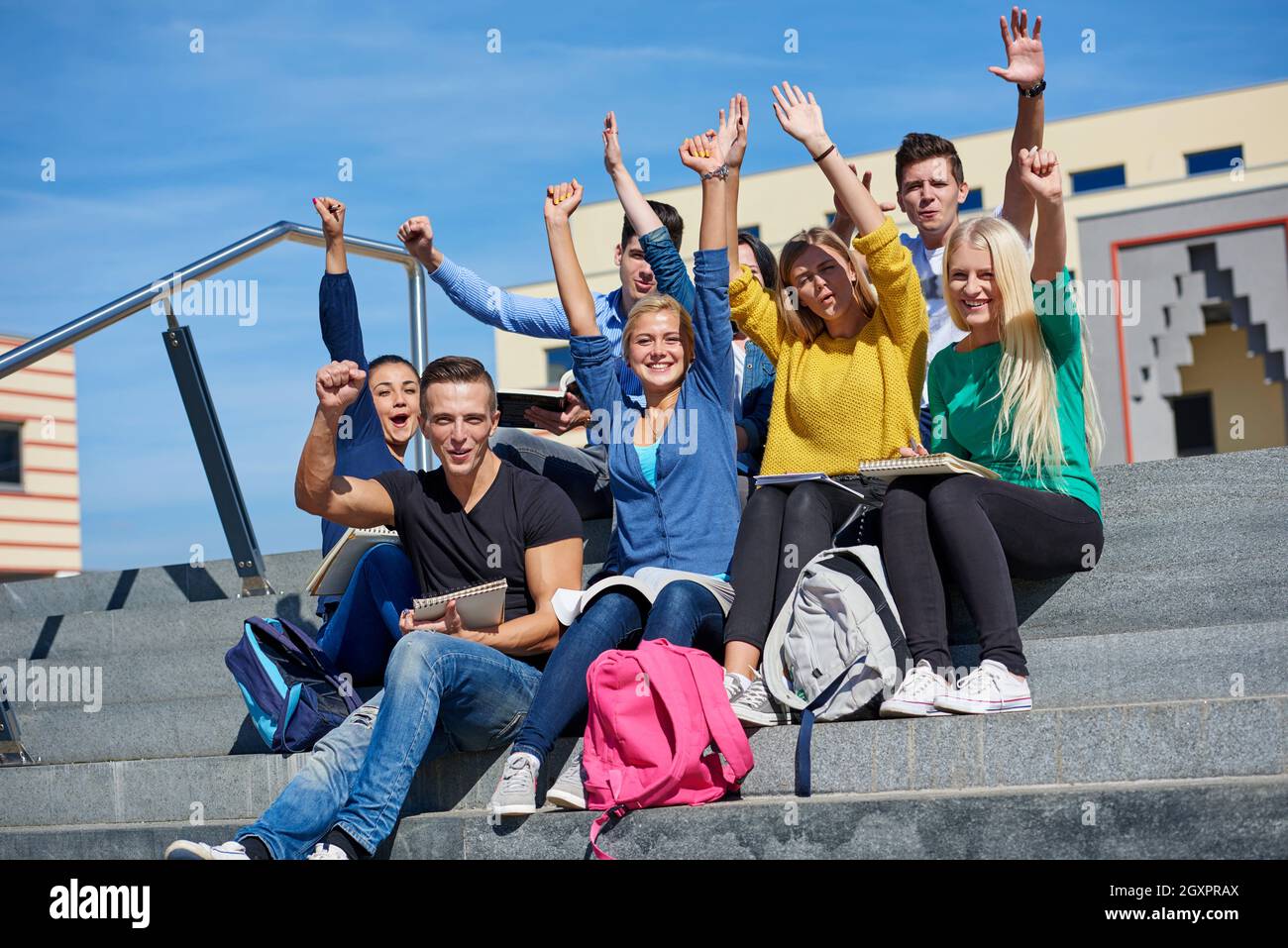 Group portrait of happy students outside in front of school sitting on ...