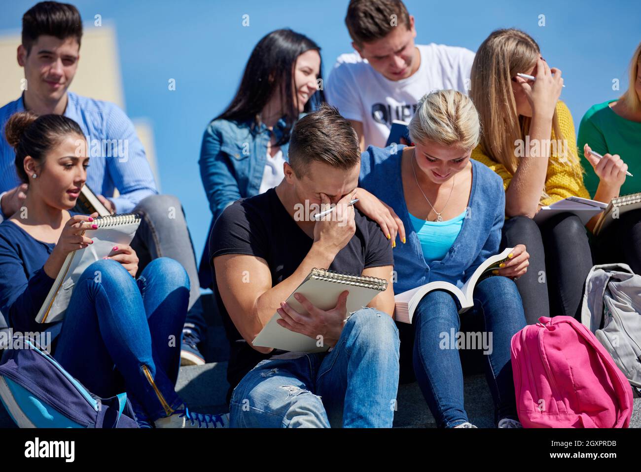 Group portrait of happy students outside in front of school sitting on ...