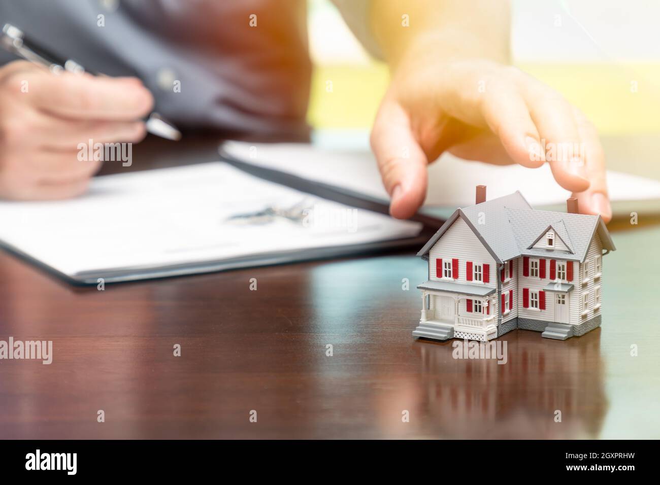 Man signing real estate contract papers and reaching for small model ...