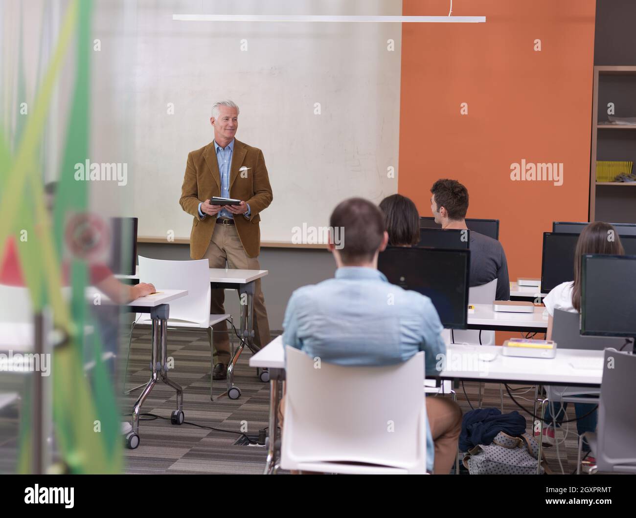 Handsome senior teacher and students group in computer lab classroom ...