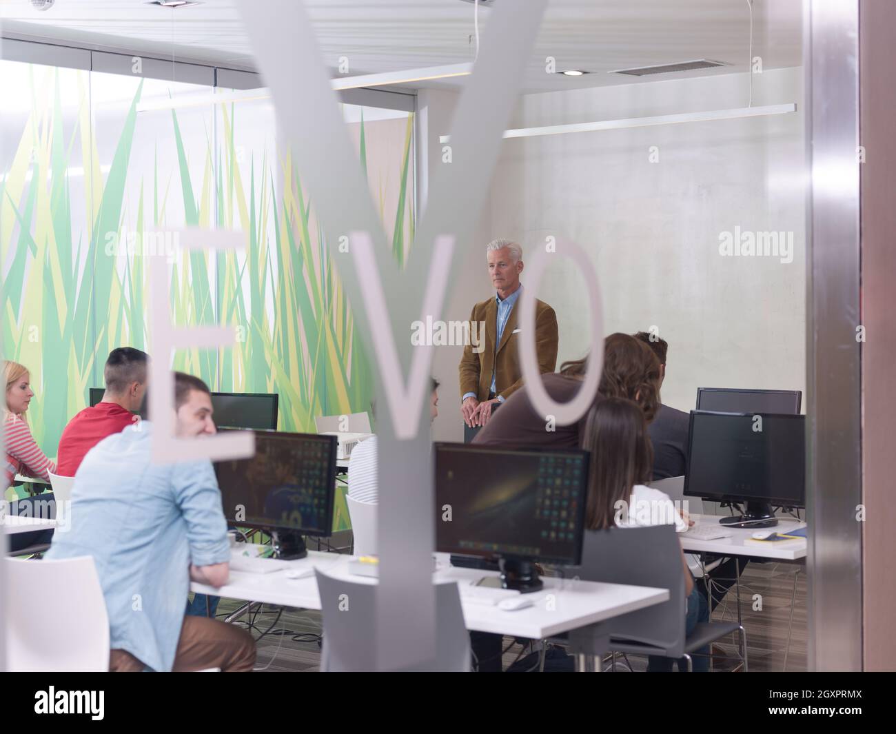 Handsome senior teacher and students group in computer lab classroom ...