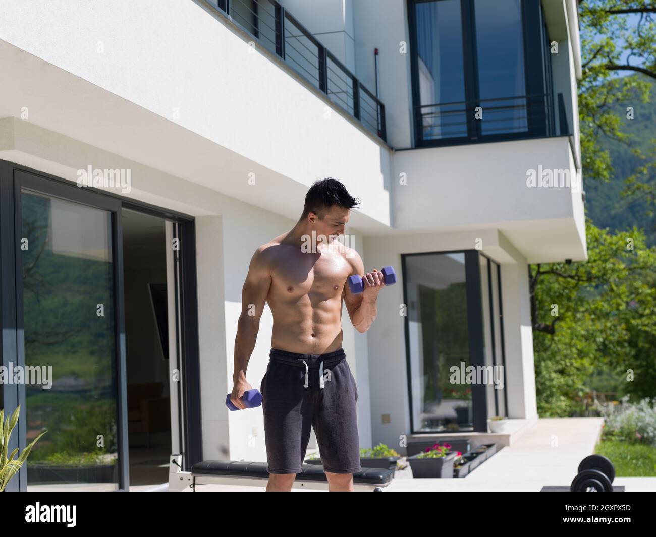 young handsome man doing morning exercises in front of his luxury home ...