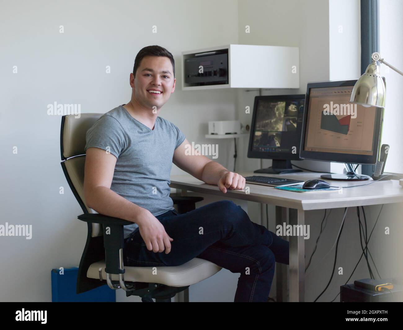 portrait of security system operator looking at CCTV footage at desk in ...