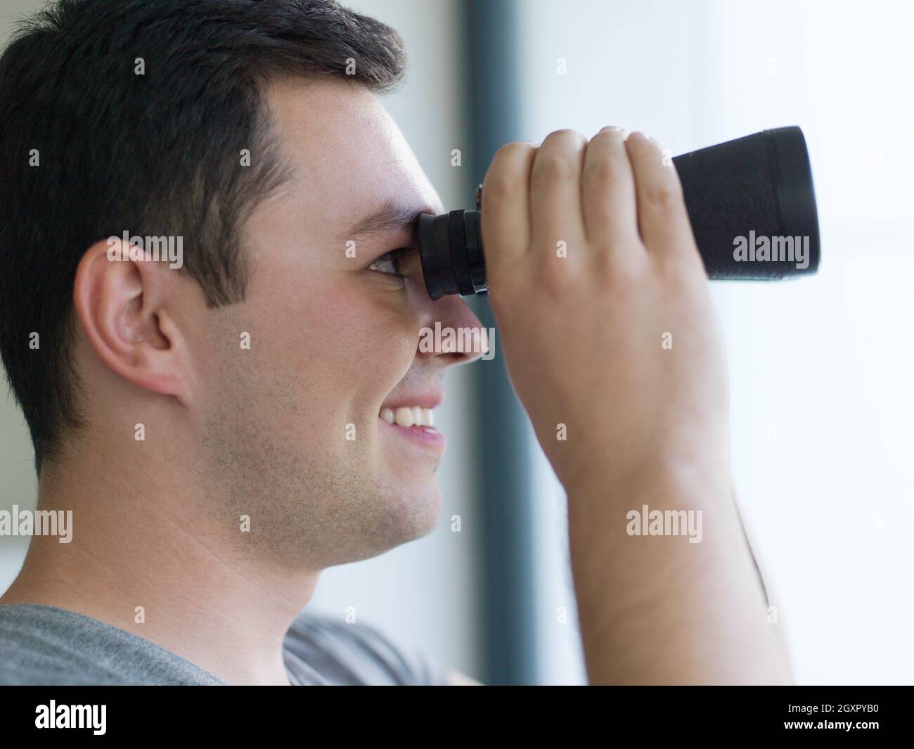 Young man standing looking through a glass window with binoculars as he ...