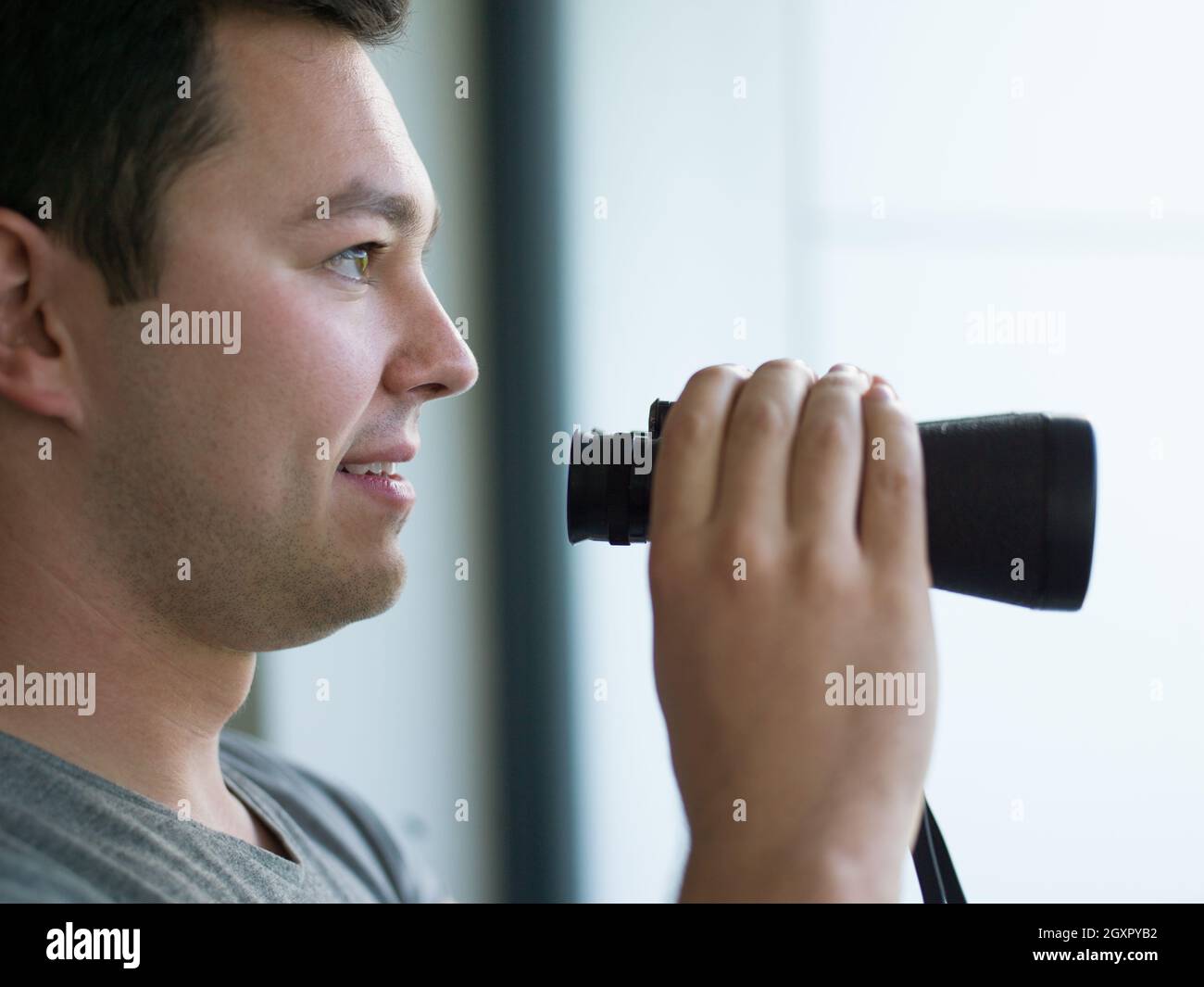 Young man standing looking through a glass window with binoculars as he ...