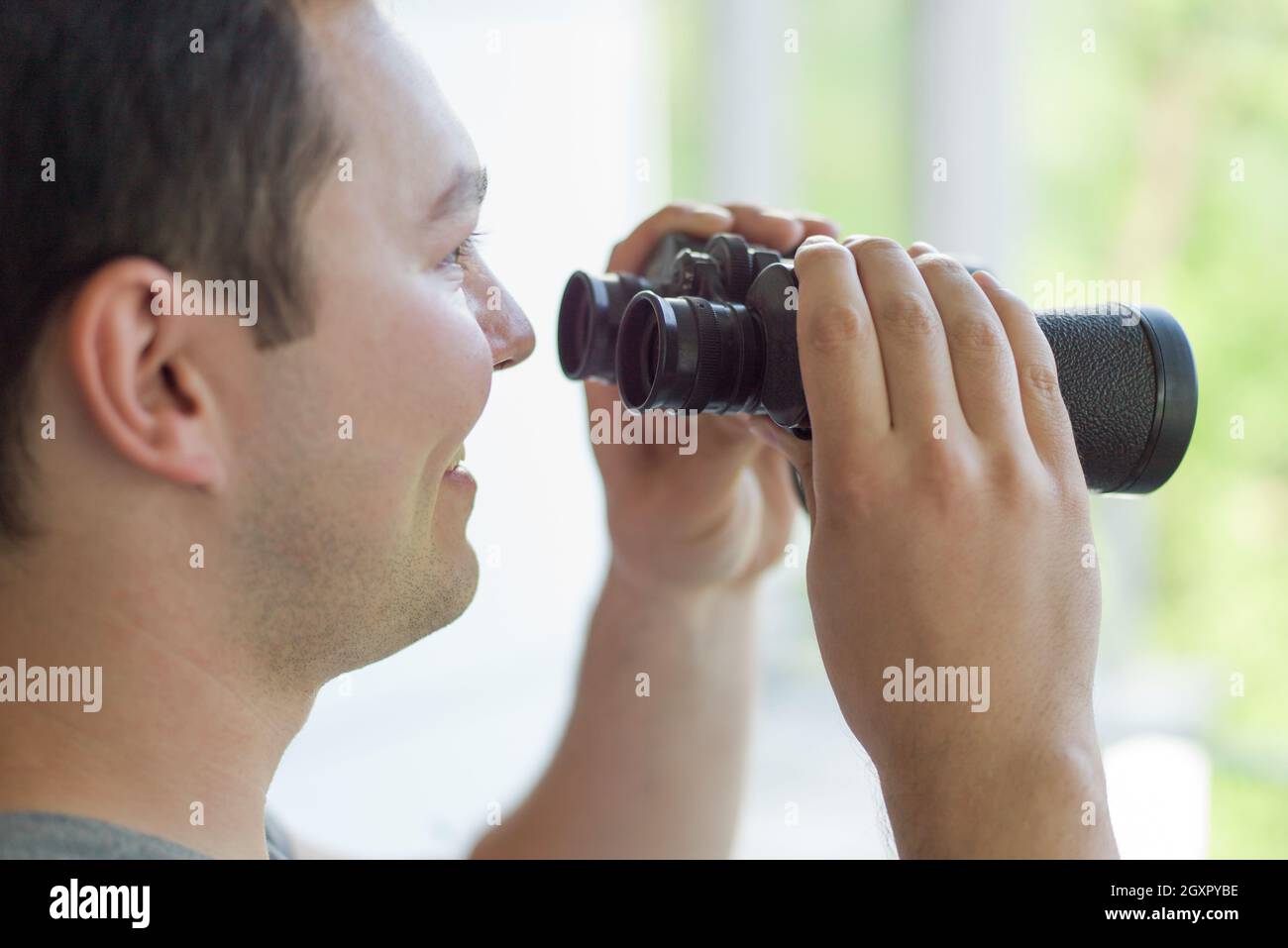Young man standing looking through a glass window with binoculars as he ...