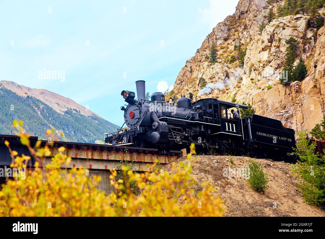 Close up of locomotive train approaching bridge with fall colors and ...