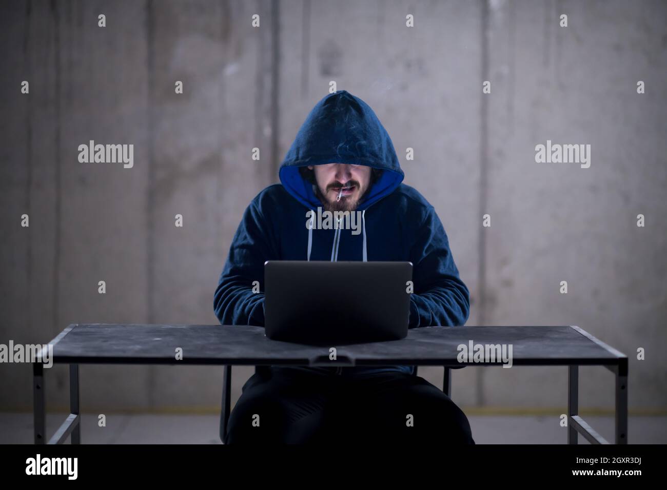 Young talented hacker smoking cigarette while working on laptop ...