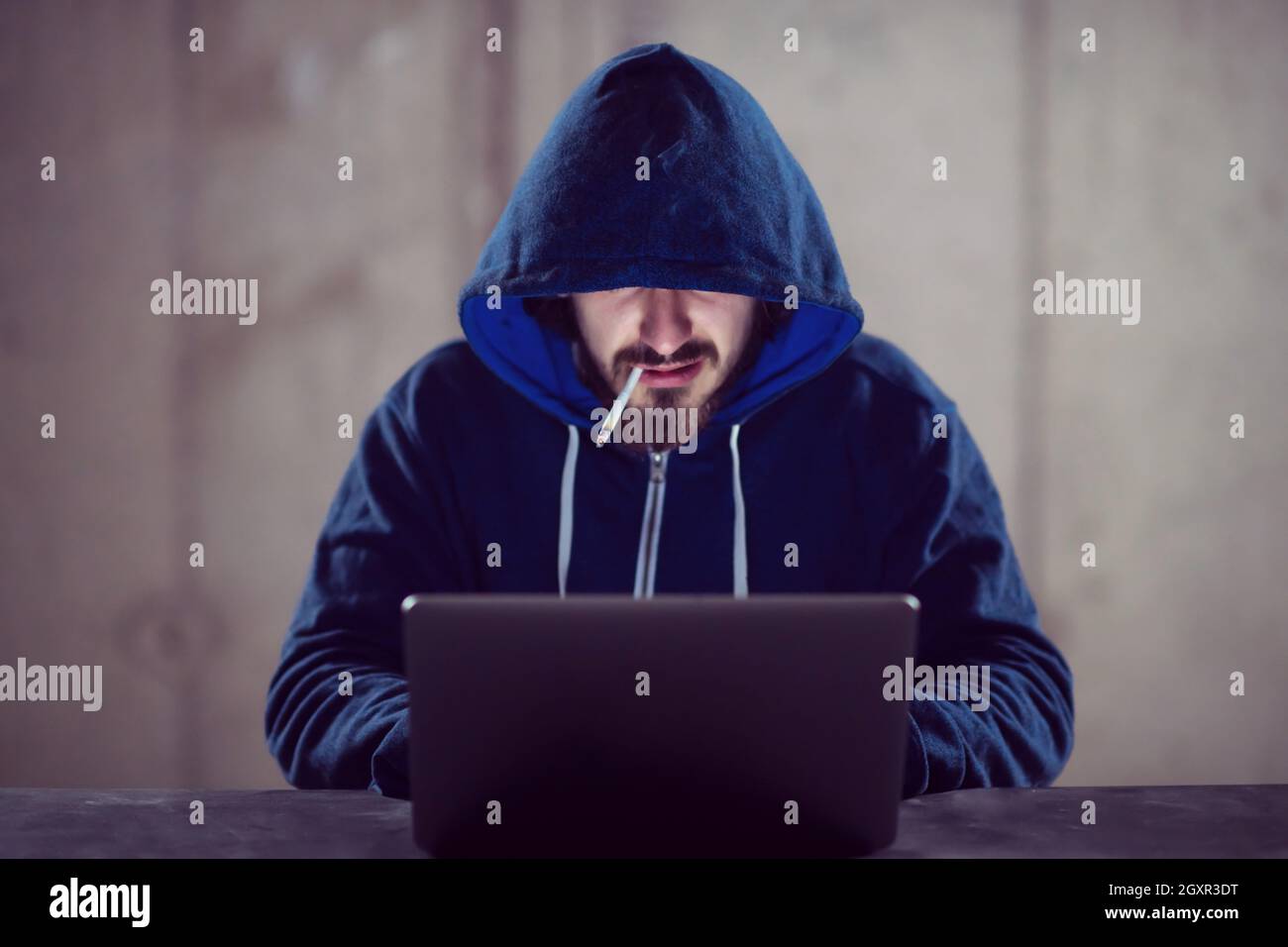 Young talented hacker smoking cigarette while working on laptop ...