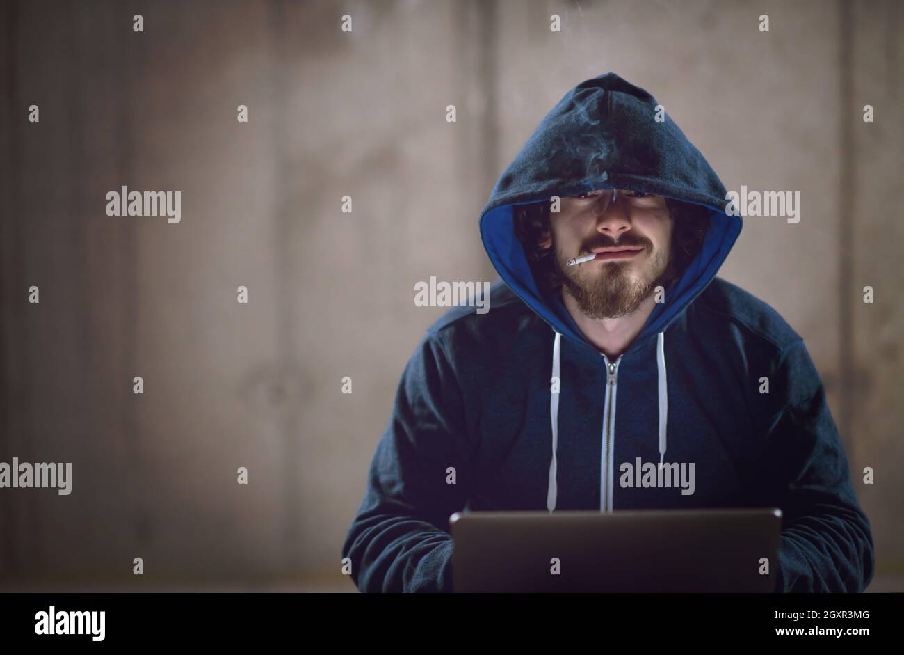 Young talented hacker smoking cigarette while working on laptop ...