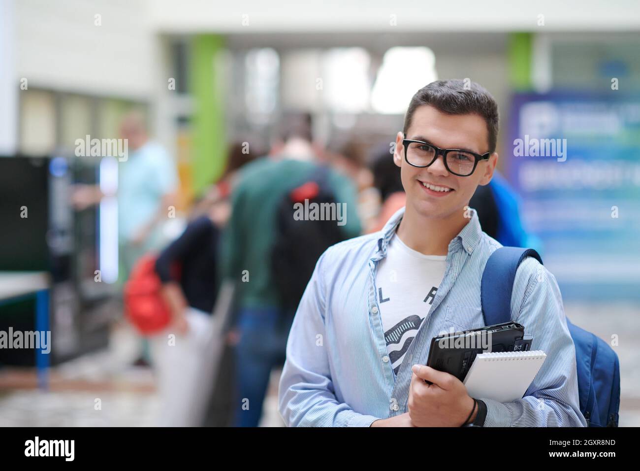 a student in glasses stands in the hallway of a modern college and uses ...