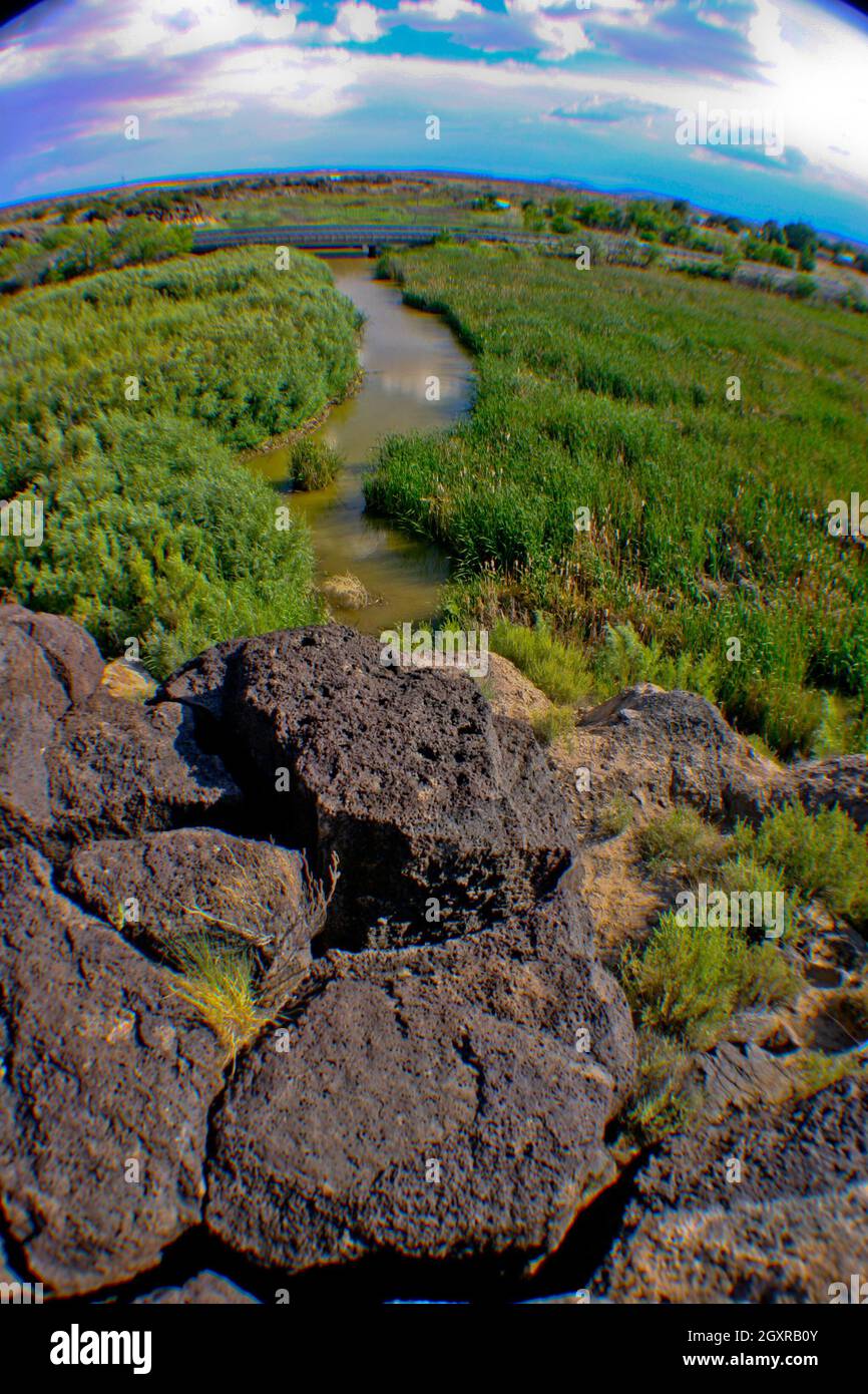 Large black rocks obscure the mouth of a river that flows through green ...
