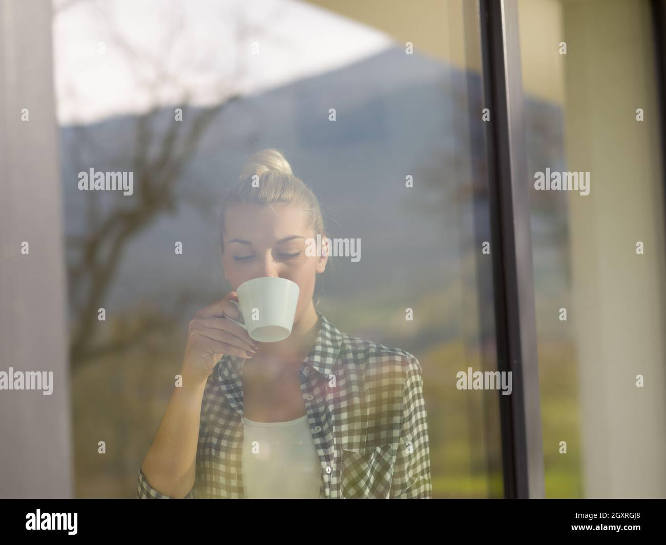 beautiful young woman drinking morning coffee by the window in her home ...
