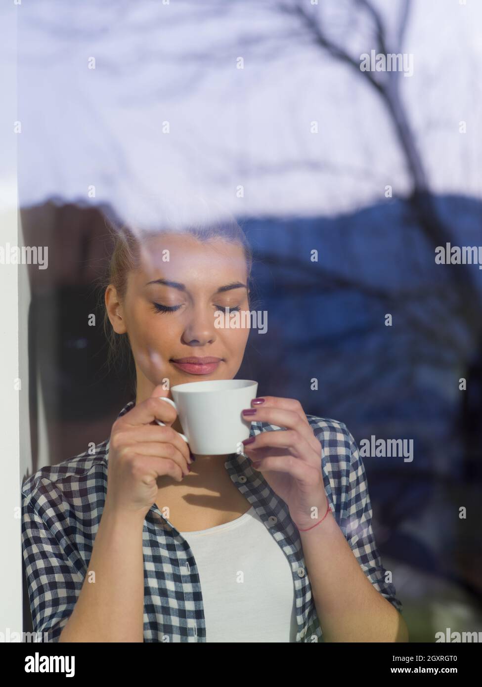beautiful young woman drinking morning coffee by the window in her home ...