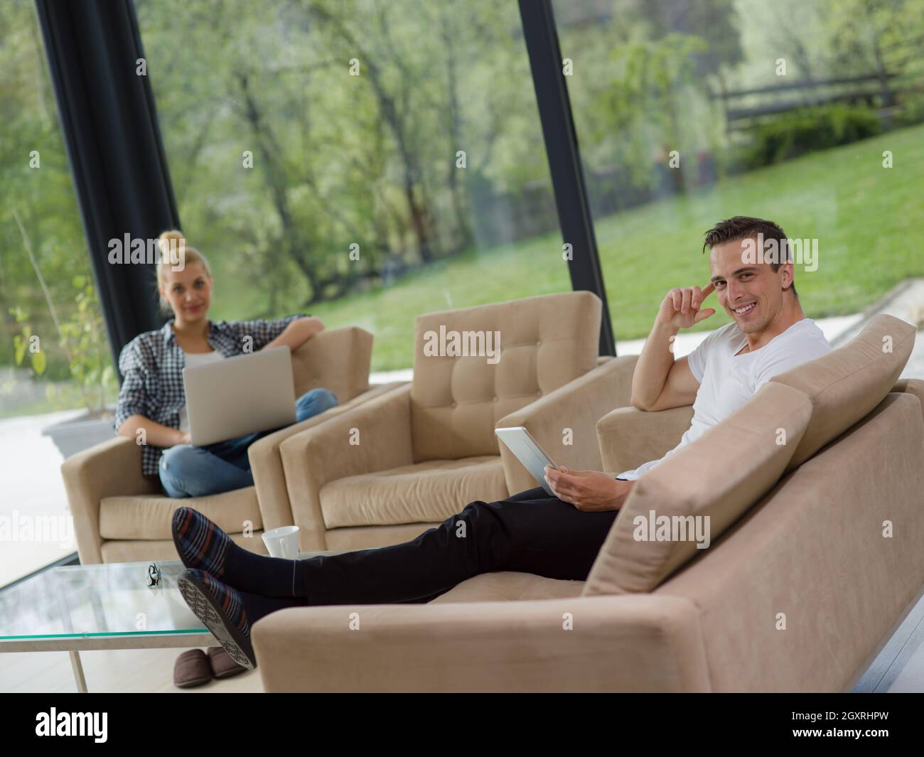Young couple relaxing at luxurious home with tablet and laptop ...