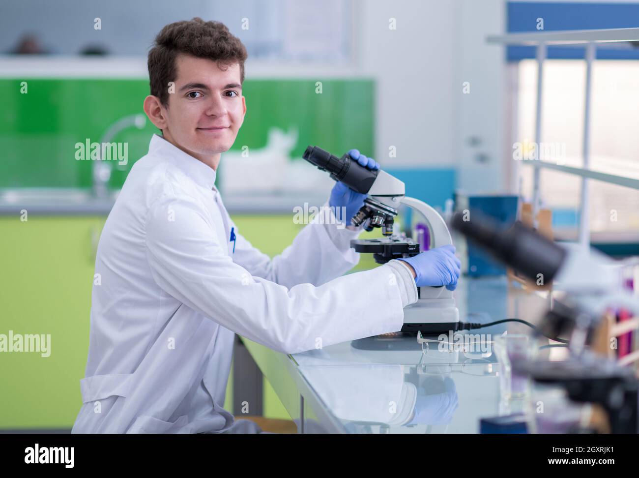 Young student scientist looking through a microscope while doing some ...