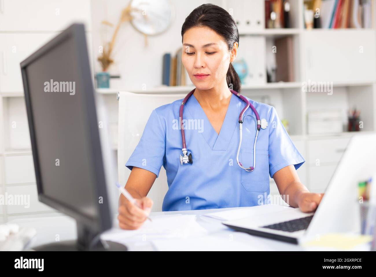 Portrait of female doctor who is working with laptop and documents ...
