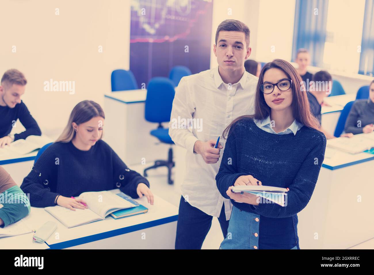 Two young students man and woman with others working on a project in a ...