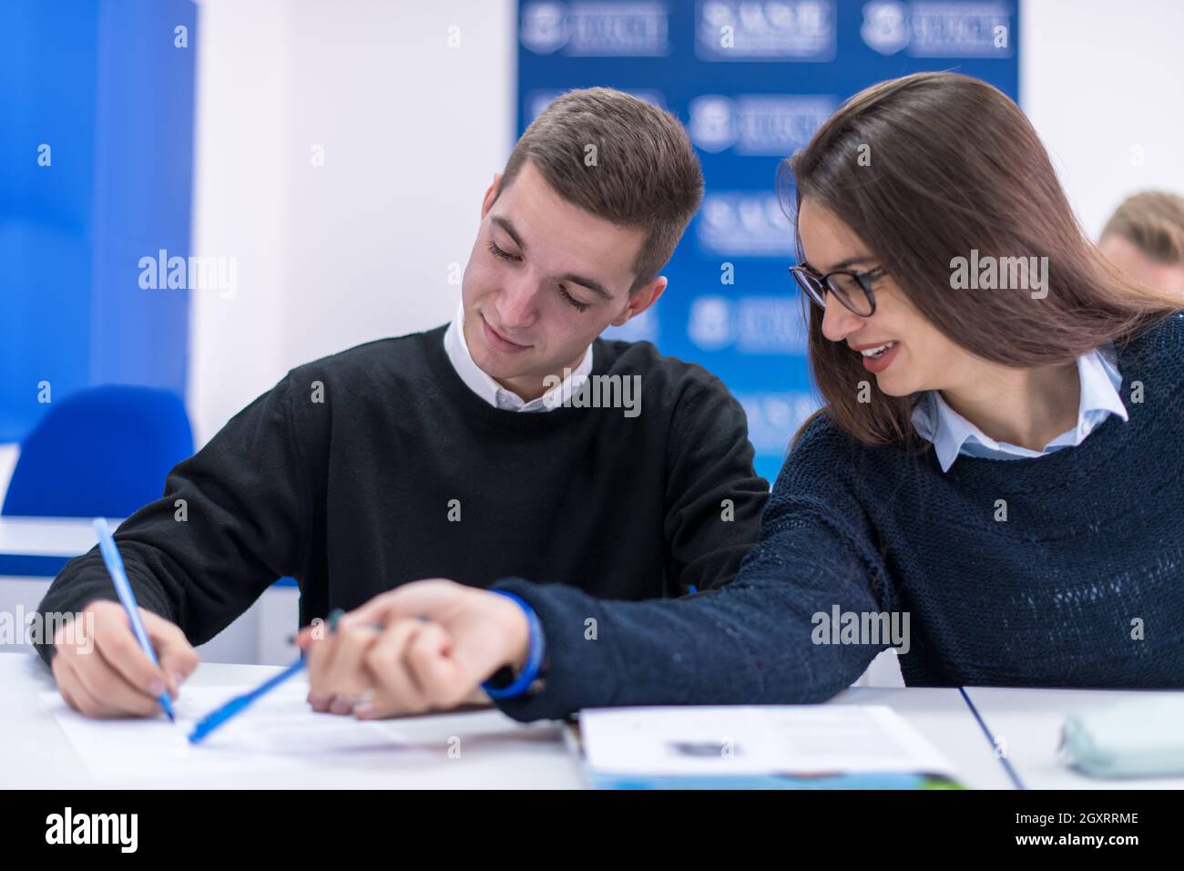 Two young students man and woman with others working on a project in a ...
