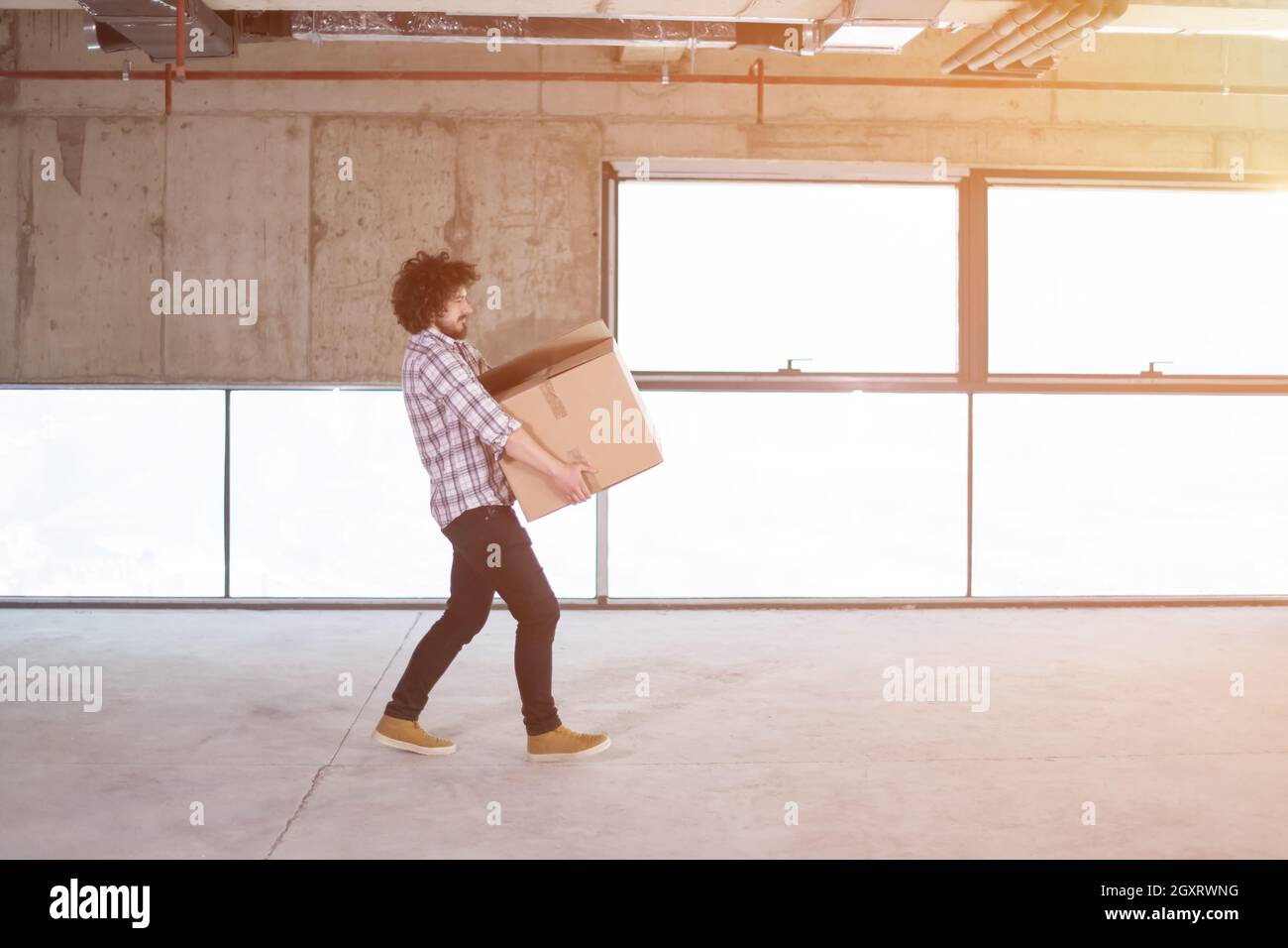happy young casual business man carrying cardboard box with sunlight ...