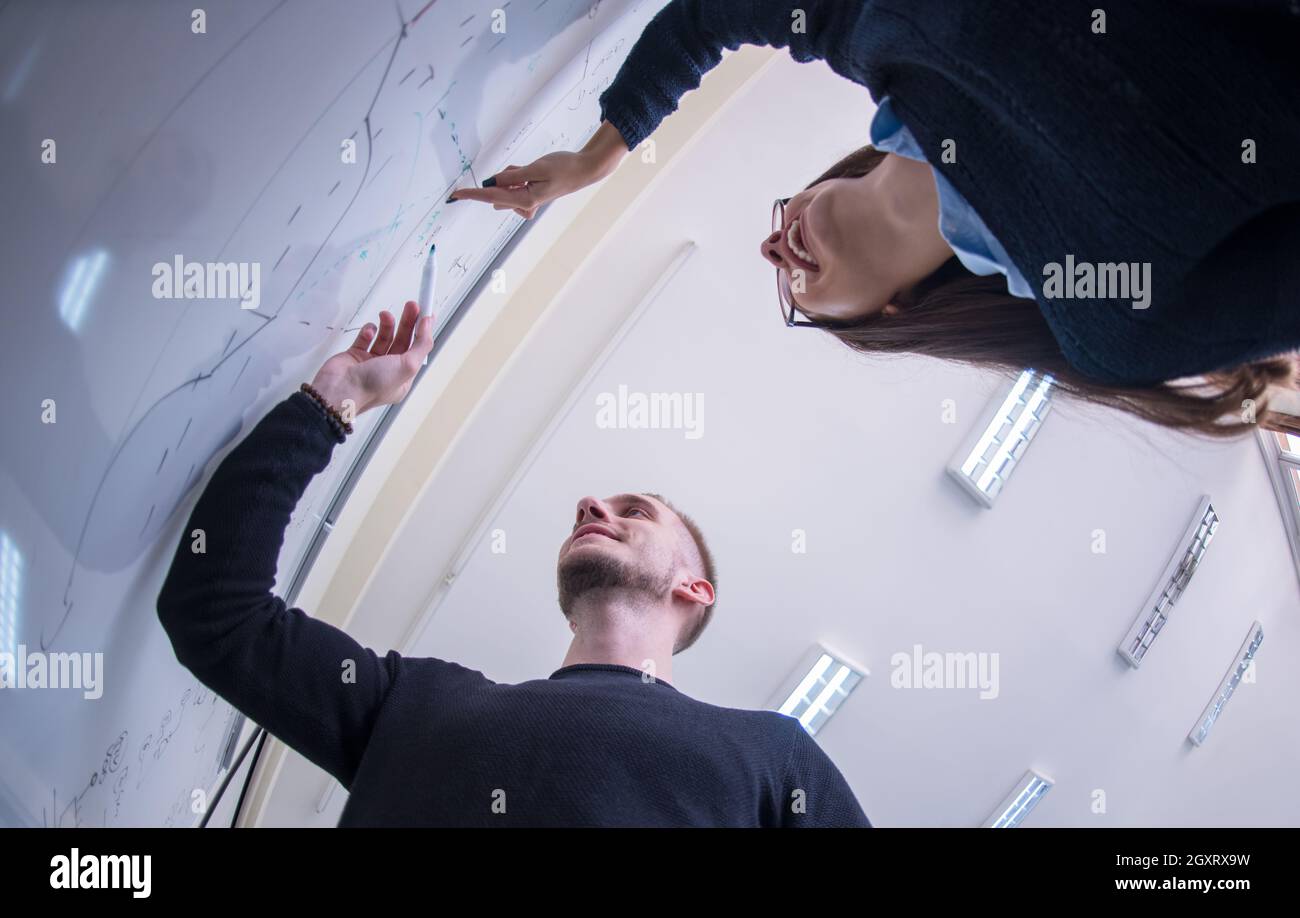 Two young male and female students writing on the white chalkboard ...