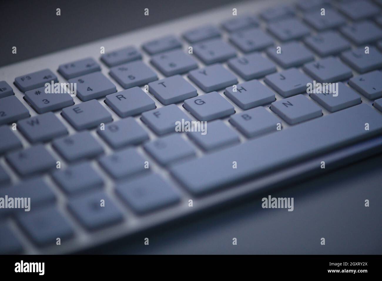 slim white minimalistic keyboard close up in dark night lit by screen ...
