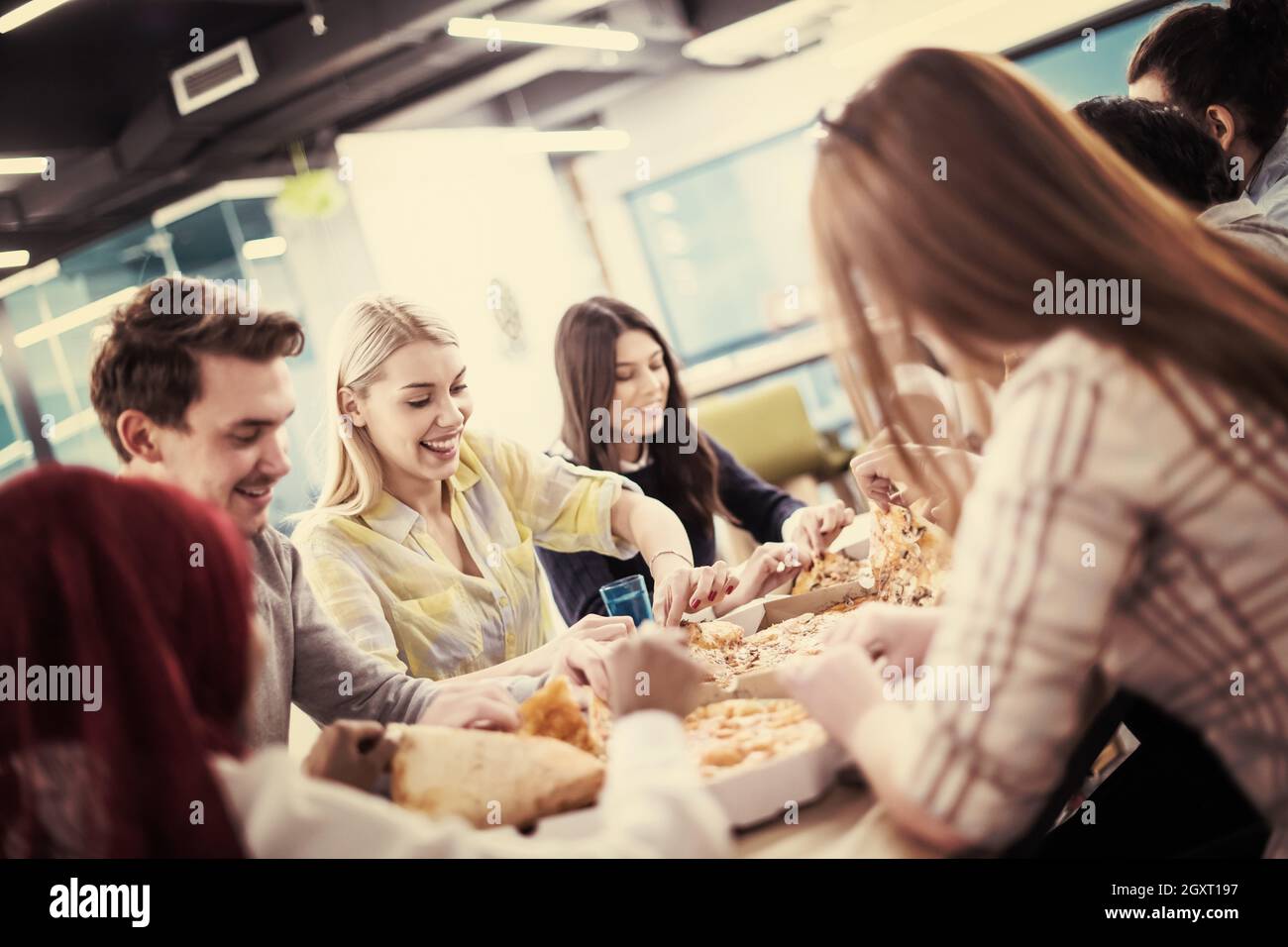 Friendly diverse multiethnic business team eating sharing pizza together in startup office ...