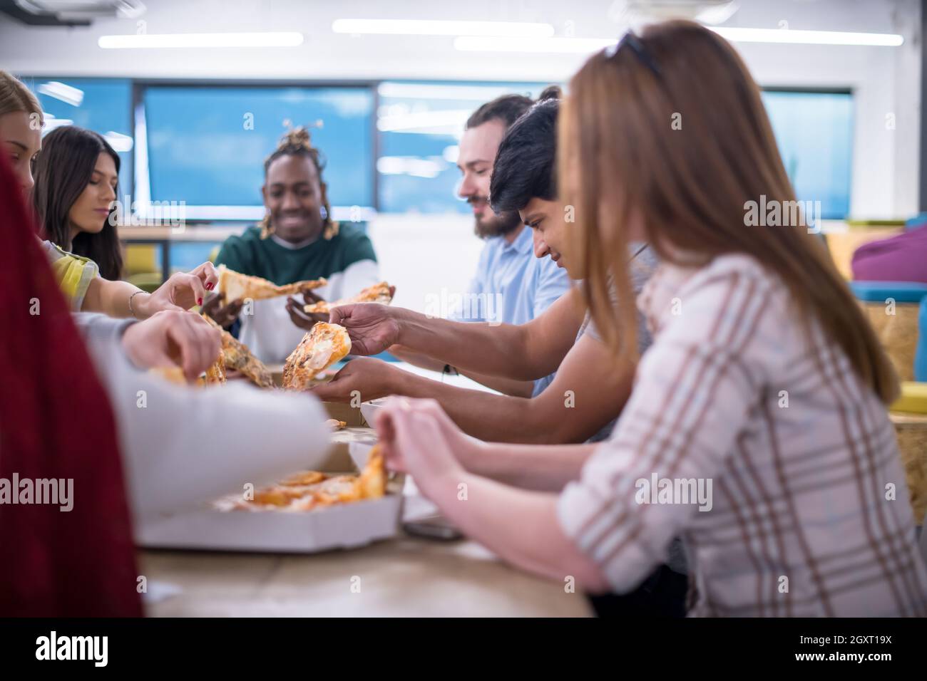 Friendly diverse multiethnic business team eating sharing pizza together in startup office ...