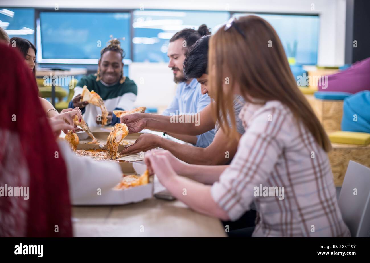 Friendly diverse multiethnic business team eating sharing pizza together in startup office ...