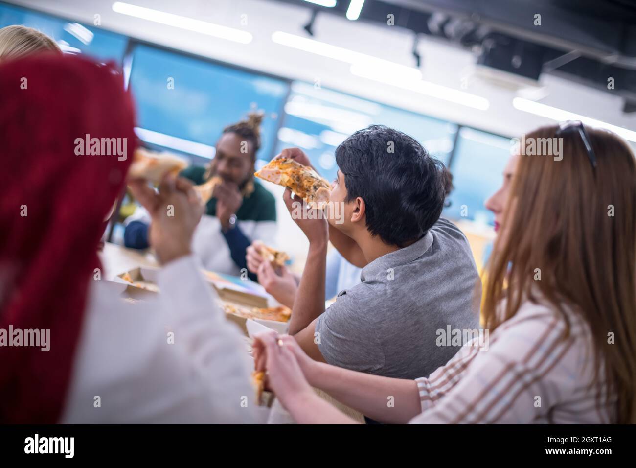 Friendly diverse multiethnic business team eating sharing pizza together in startup office ...