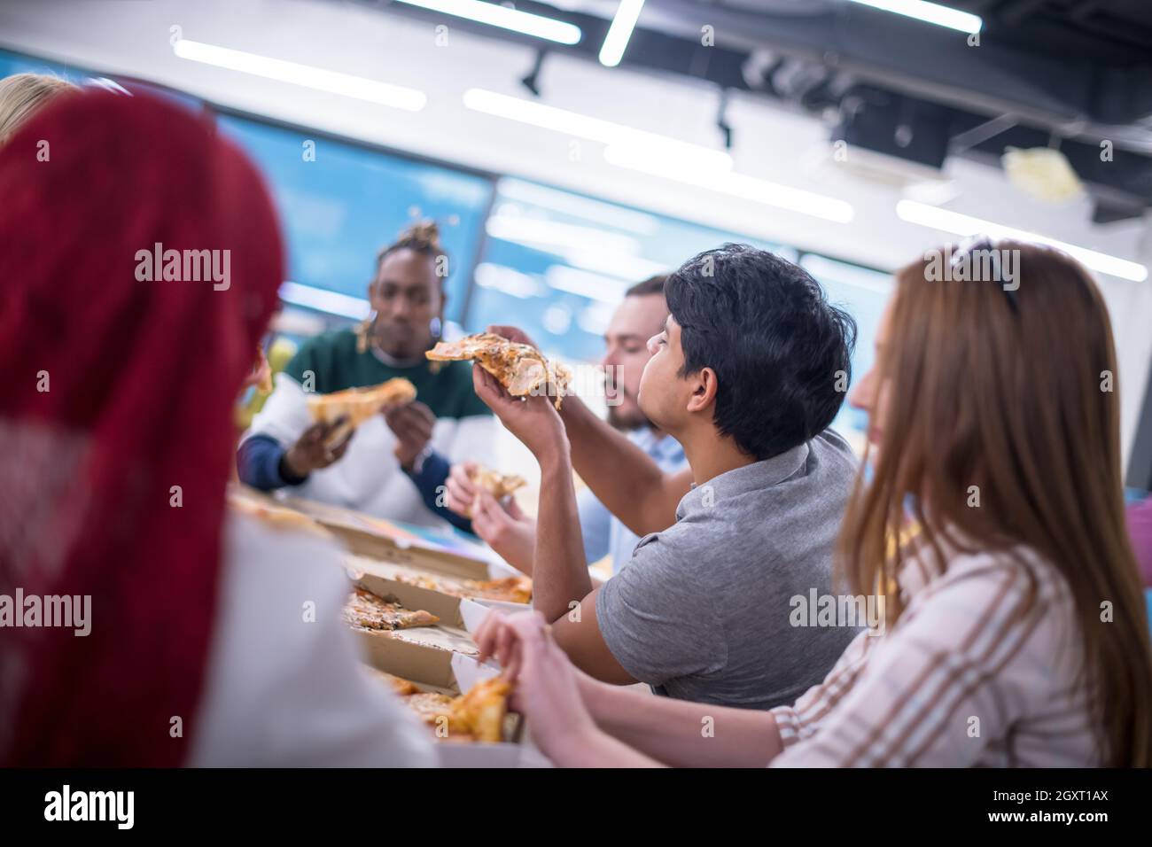 Friendly diverse multiethnic business team eating sharing pizza together in startup office ...