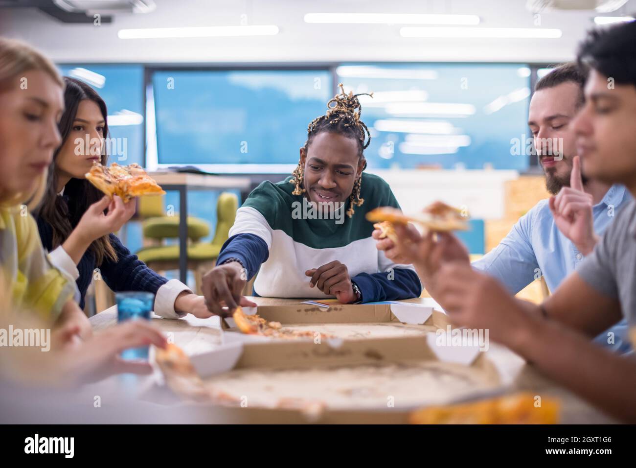 Friendly diverse multiethnic business team eating sharing pizza together in startup office ...