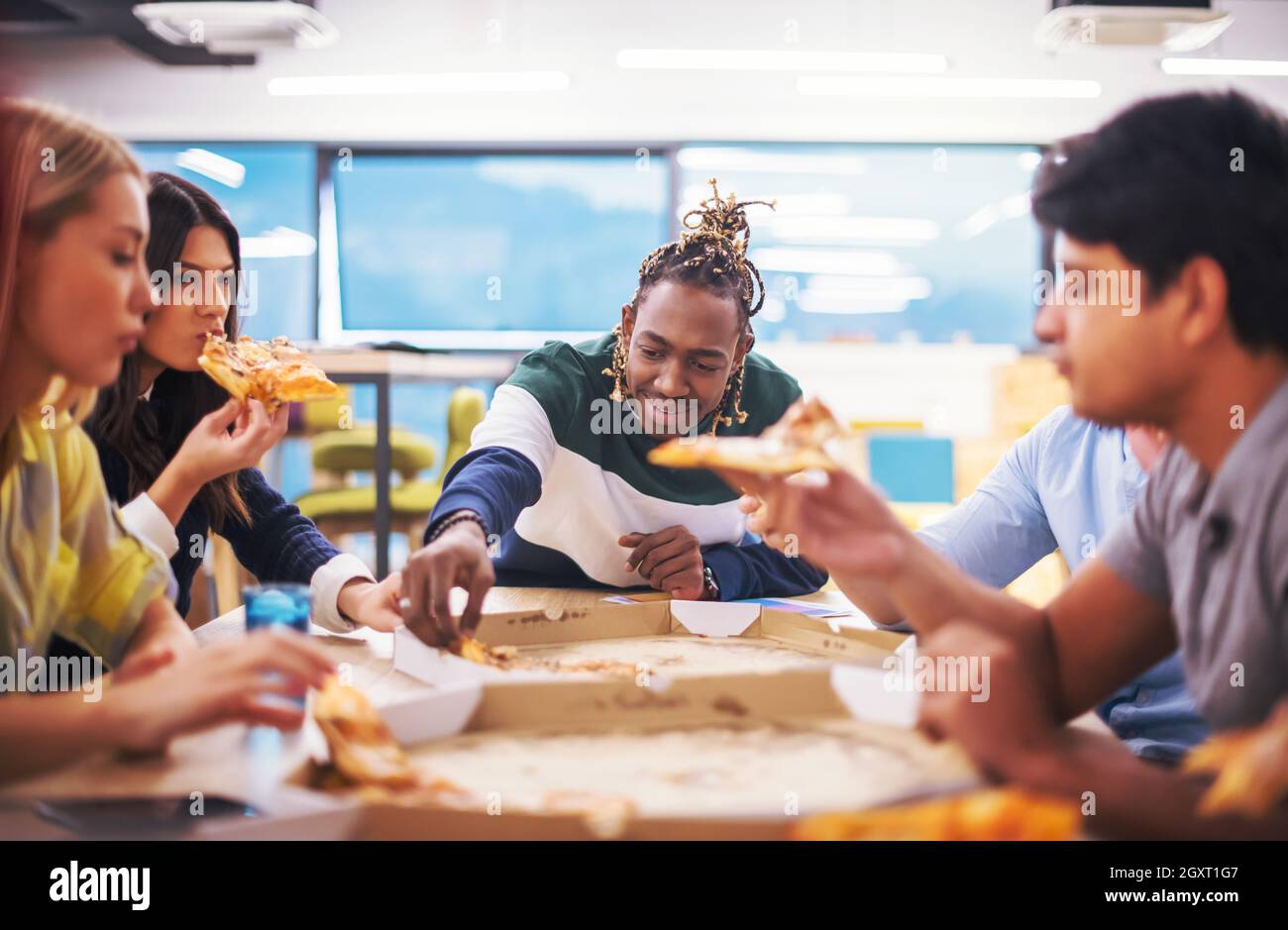 Friendly diverse multiethnic business team eating sharing pizza together in startup office ...