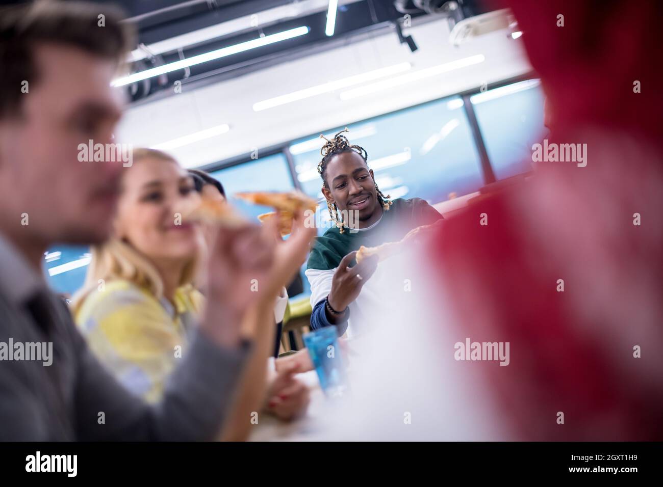 Friendly diverse multiethnic business team eating sharing pizza together in startup office ...