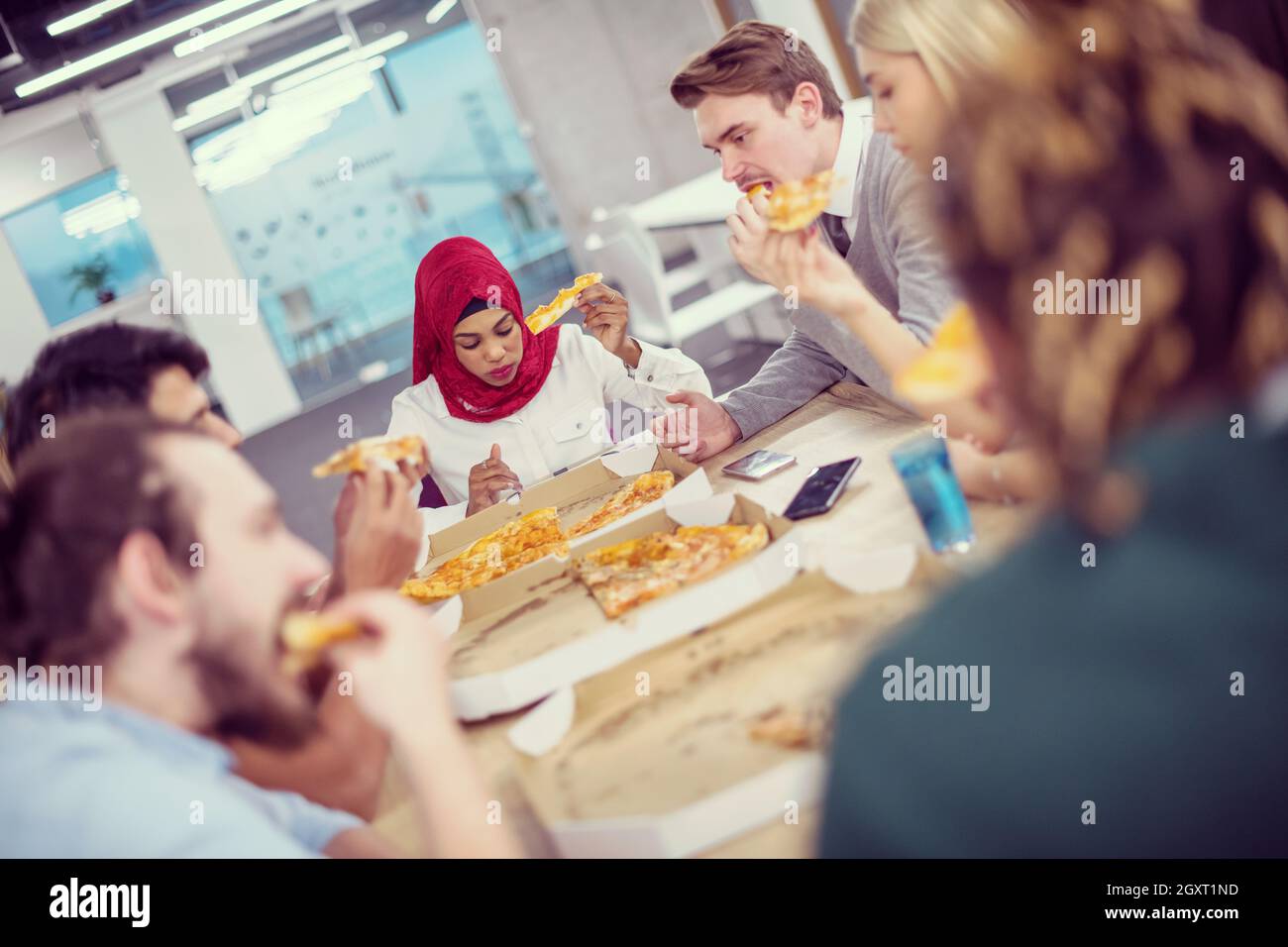 Friendly diverse multiethnic business team eating sharing pizza together in startup office ...