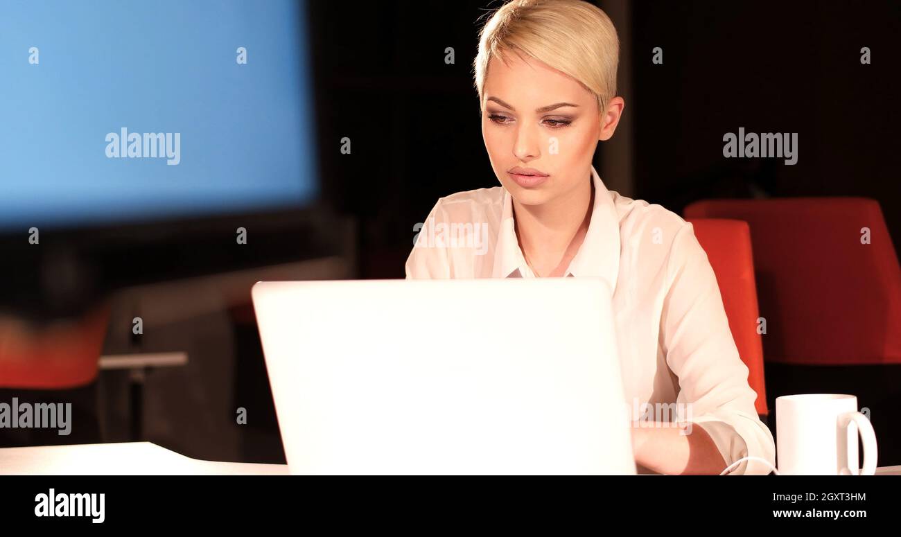 young female entrepreneur working on laptop computer in night office ...