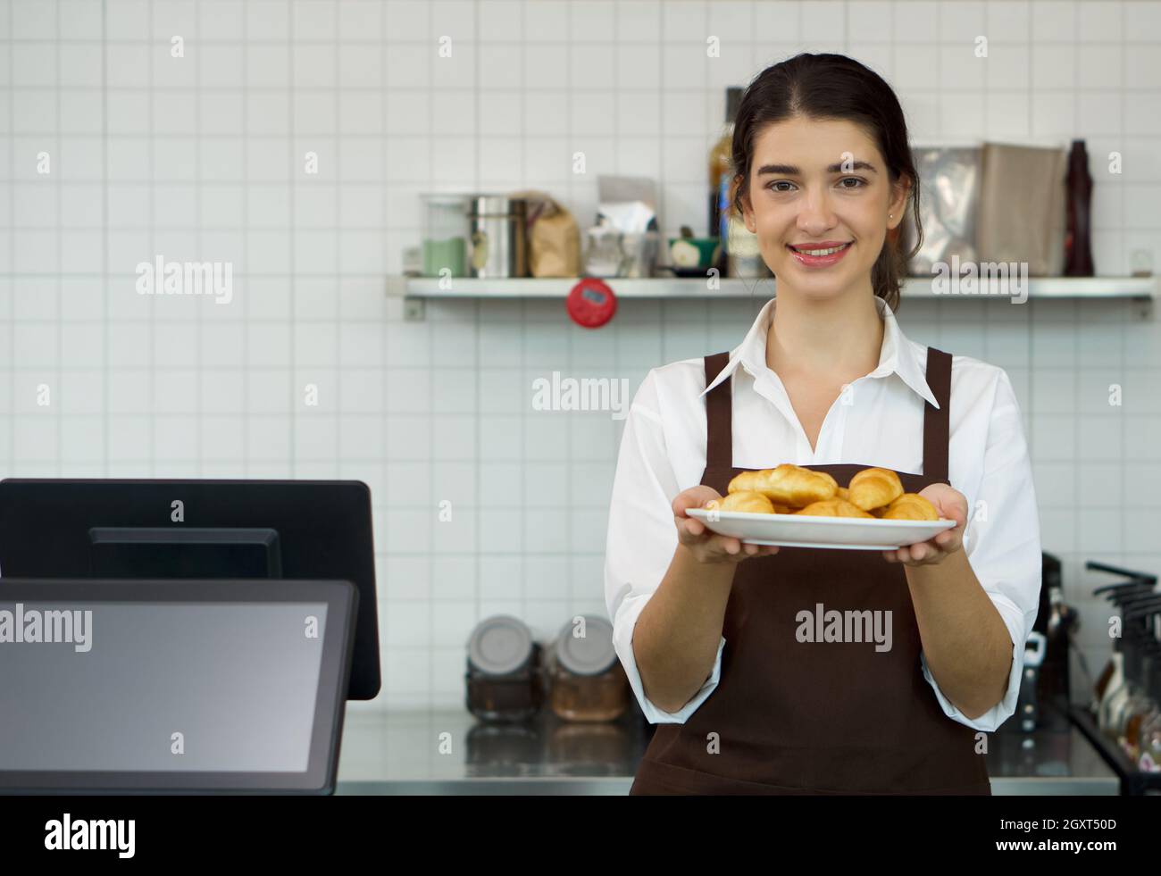 Young caucasian shopkeeper with a smile holds croissant plate in front ...