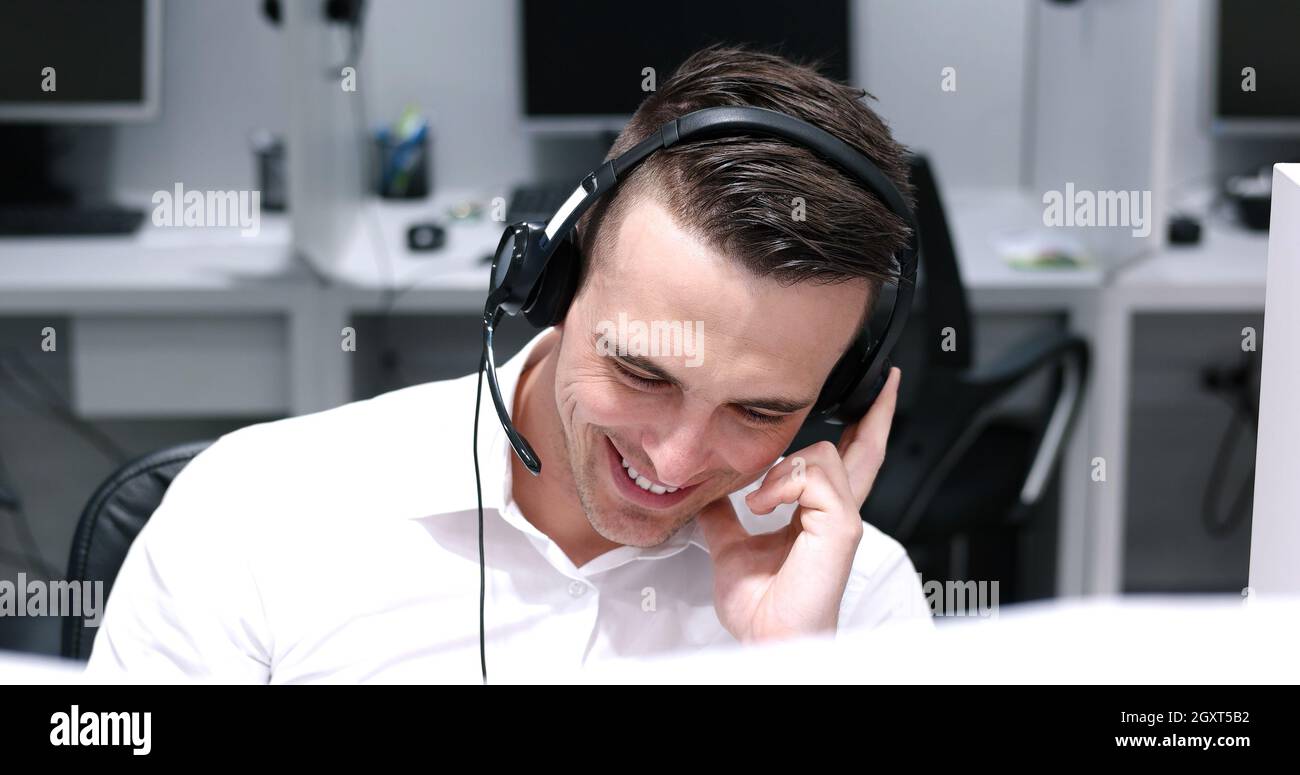 young smiling male call centre operator doing his job with a headset ...