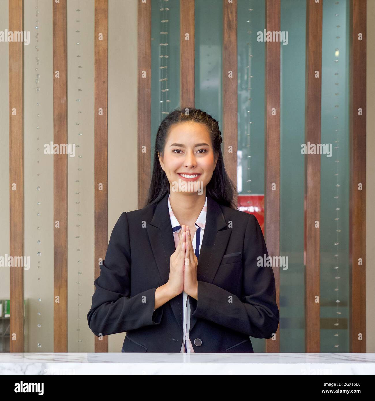 The hotel receptionist with a smile, raise her hand to pay respect in ...