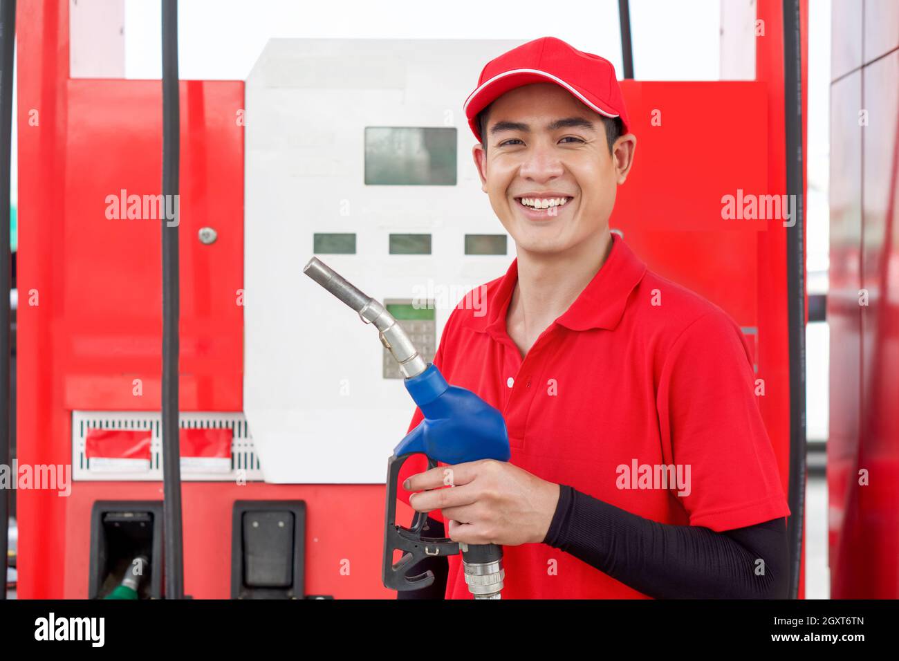 Asian gas station attendant in red uniform stand smiling, holding gas ...