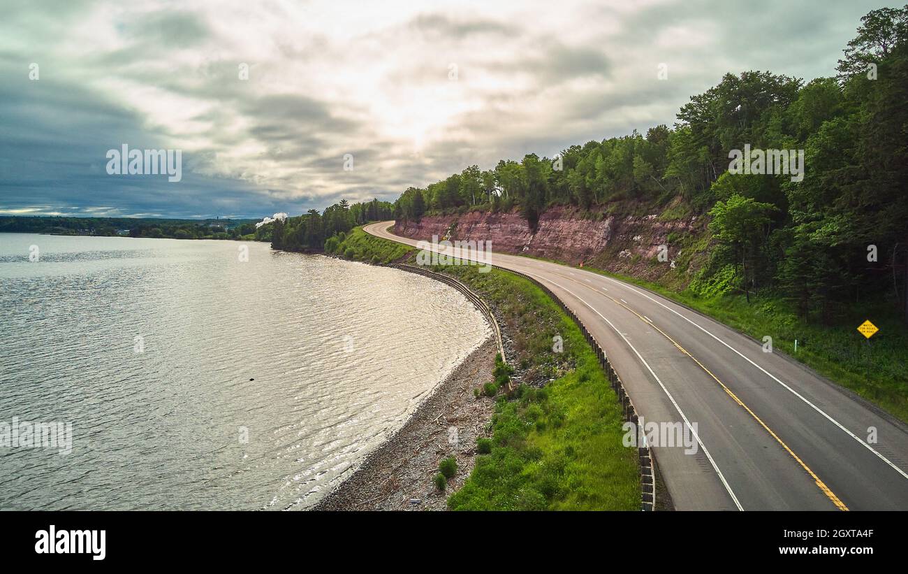 Road around large lake curving up against cliffs with dark clouds Stock ...