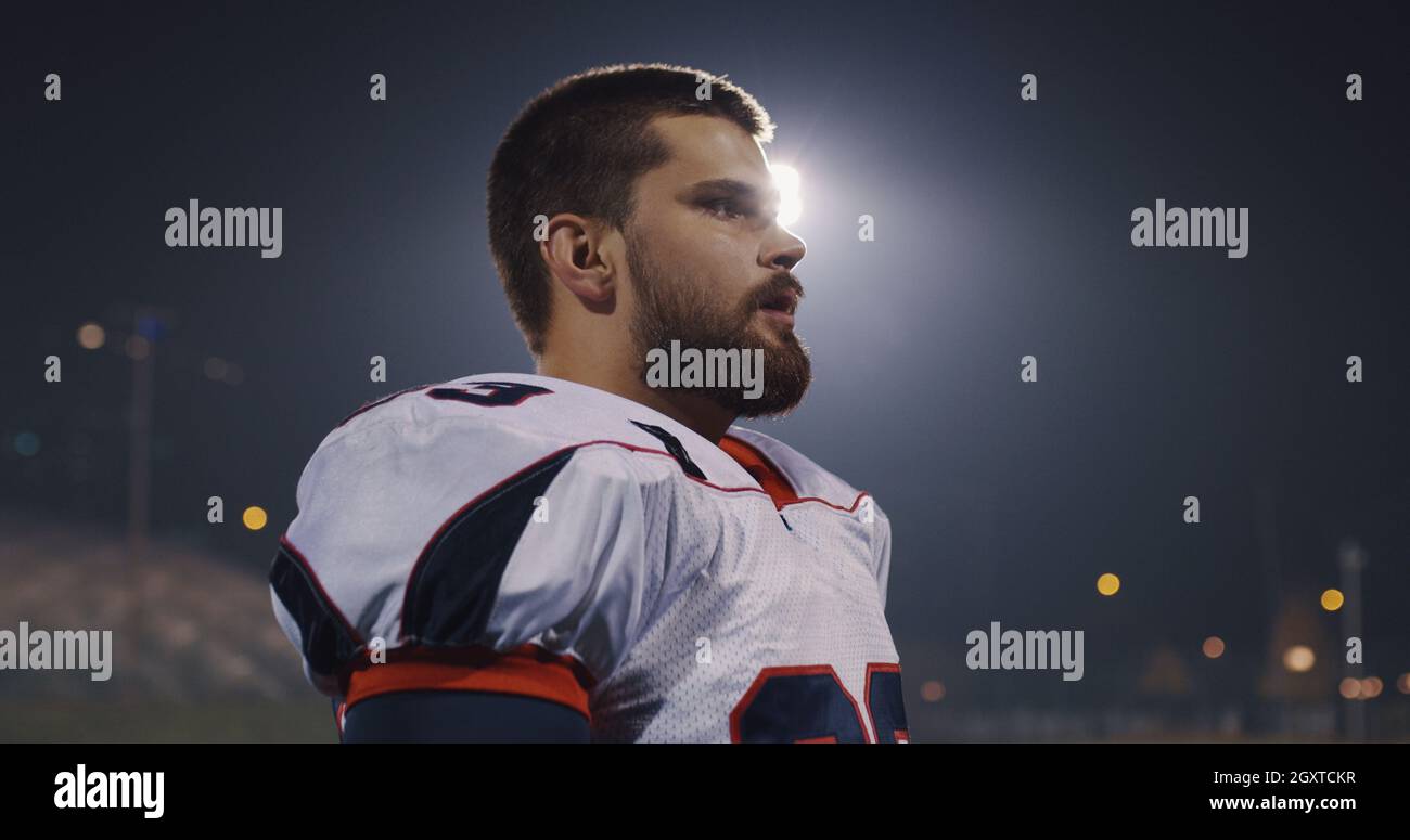 portrait of young confident American football player standing on field ...